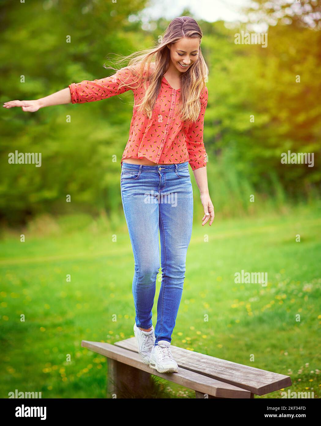 The park is her happy place. a young woman walking on a bench at the ...