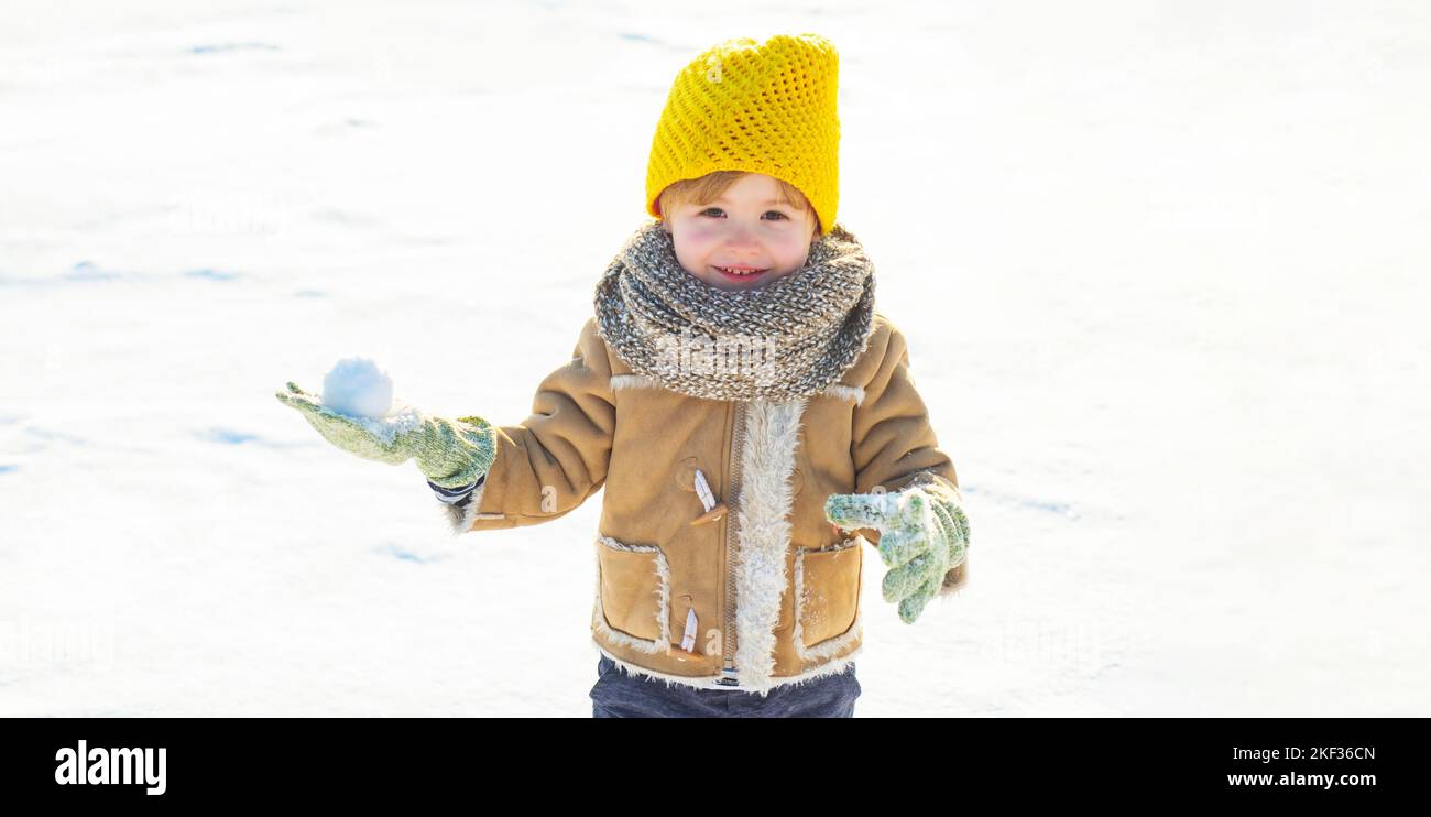 Happy child with snowball on snow background. Cute kid boy in winter ...
