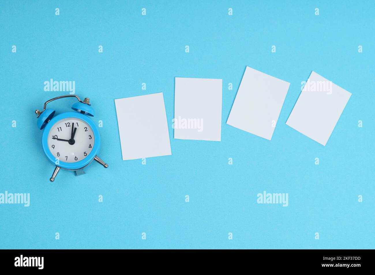 On a blue background, an alarm clock and white pieces of paper. Mockup ...
