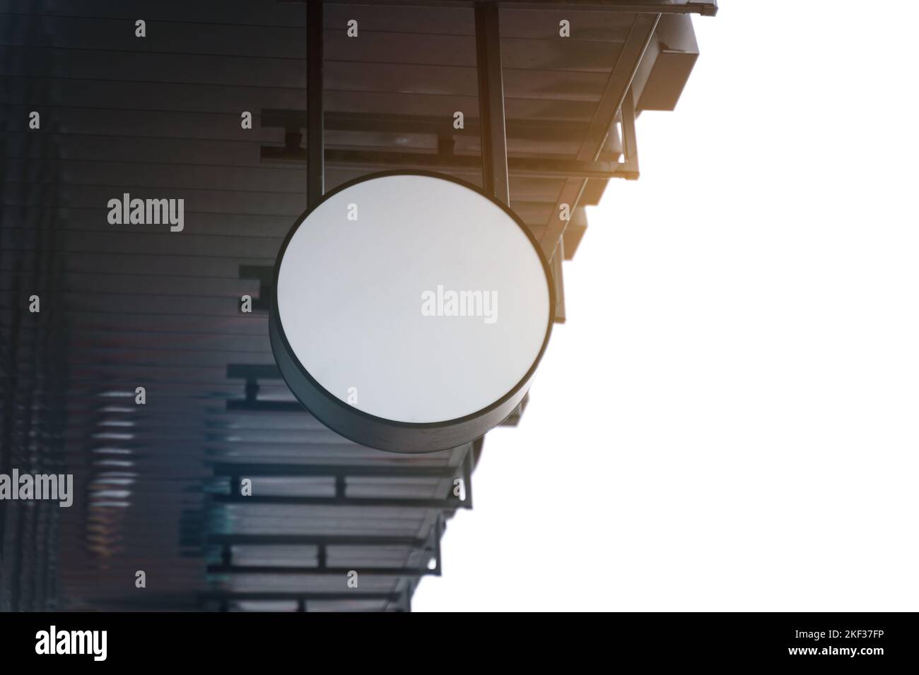 A clock with a white blank dial hangs under the roof of the building ...