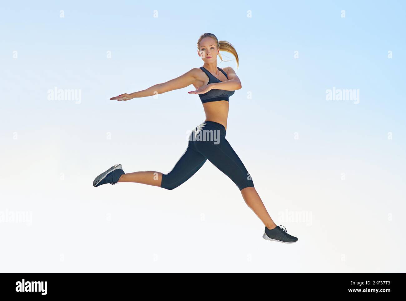 Take a leap towards fitness. Full length shot of a sporty young woman jumping against a blue sky ...