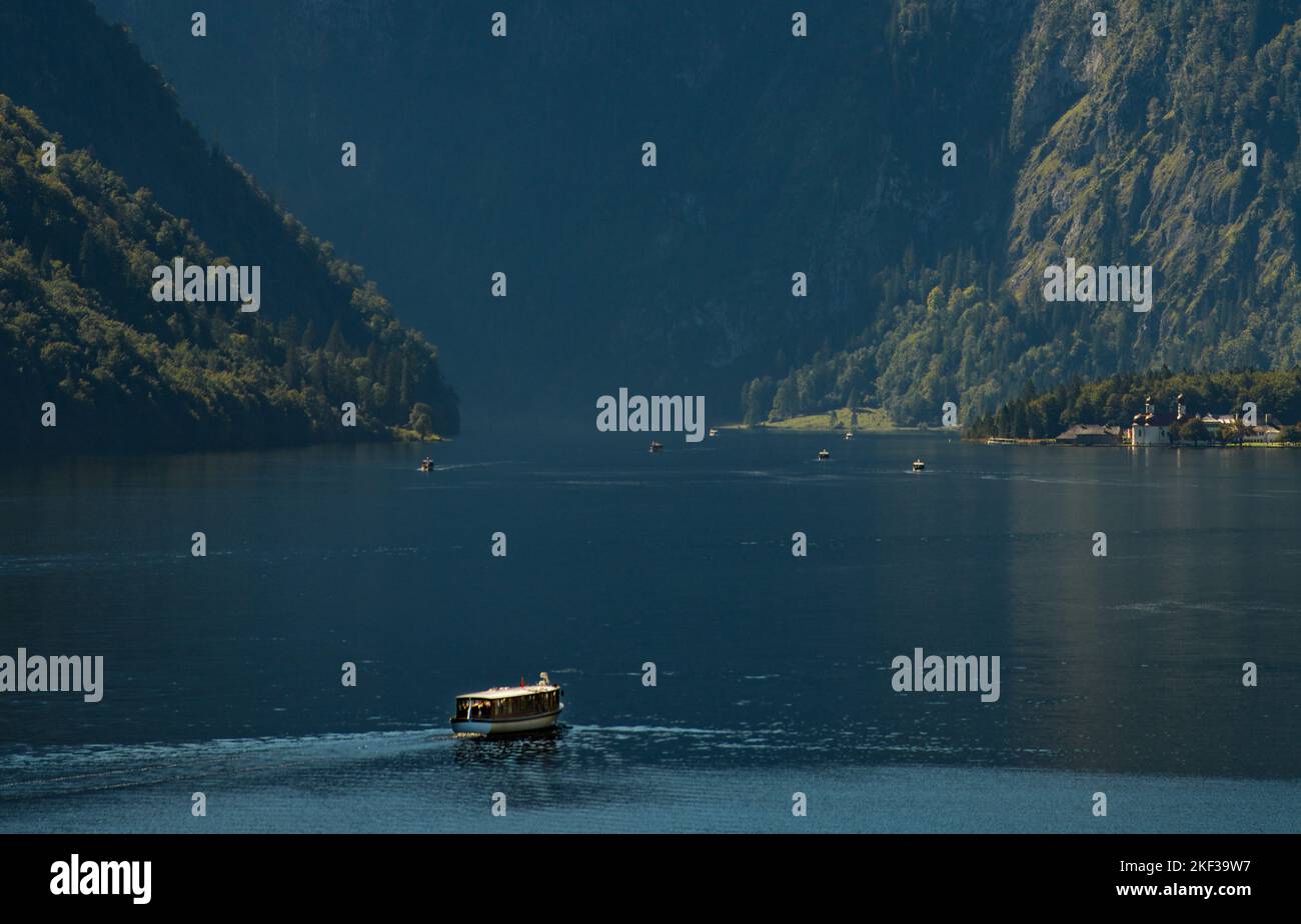 An aerial view of small boat on Konigssee lake surrounded by lush green ...