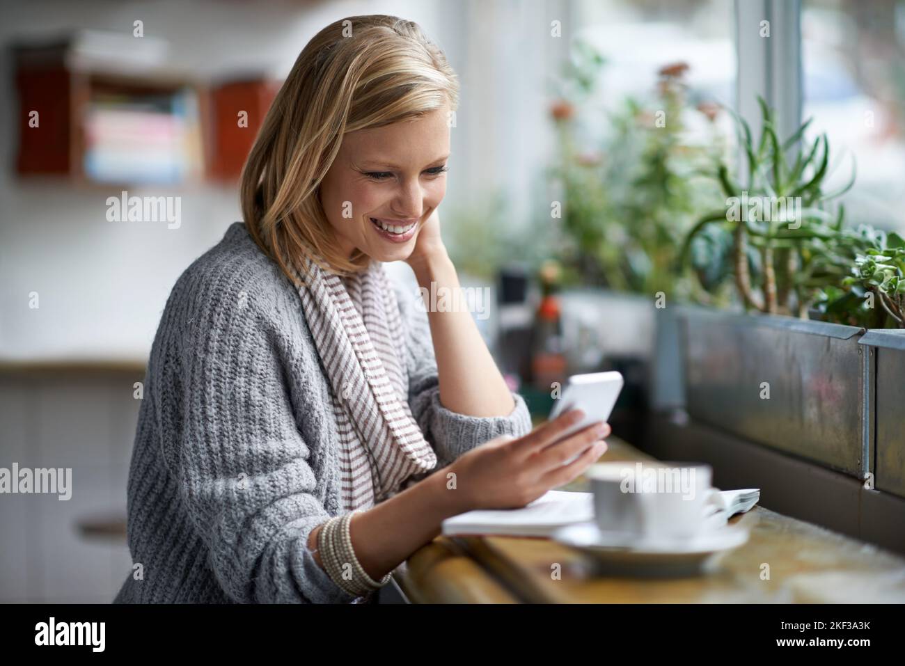 Meet me for a coffee...A young woman sitting in a coffee shop sending a ...