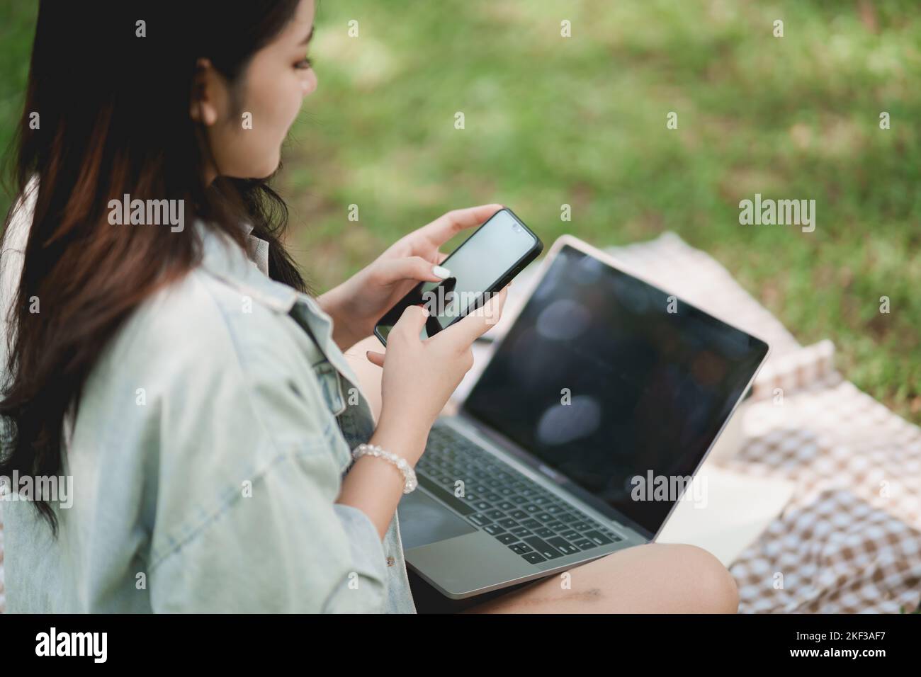 Asian woman smiling and sitting on picnic blanket and lawn at park ...