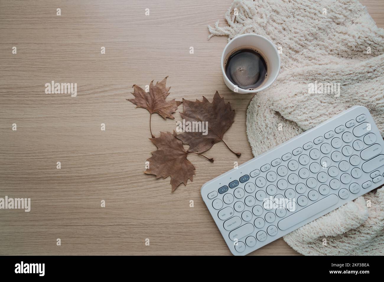 Dry maple leaves, notebook, pen and cup of coffee and white keyboard on ...