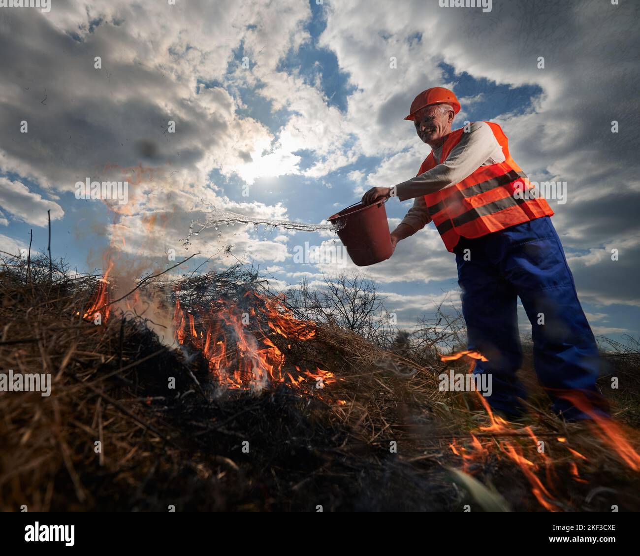 Firefighter ecologist fighting fire in field with cloudy sky on ...