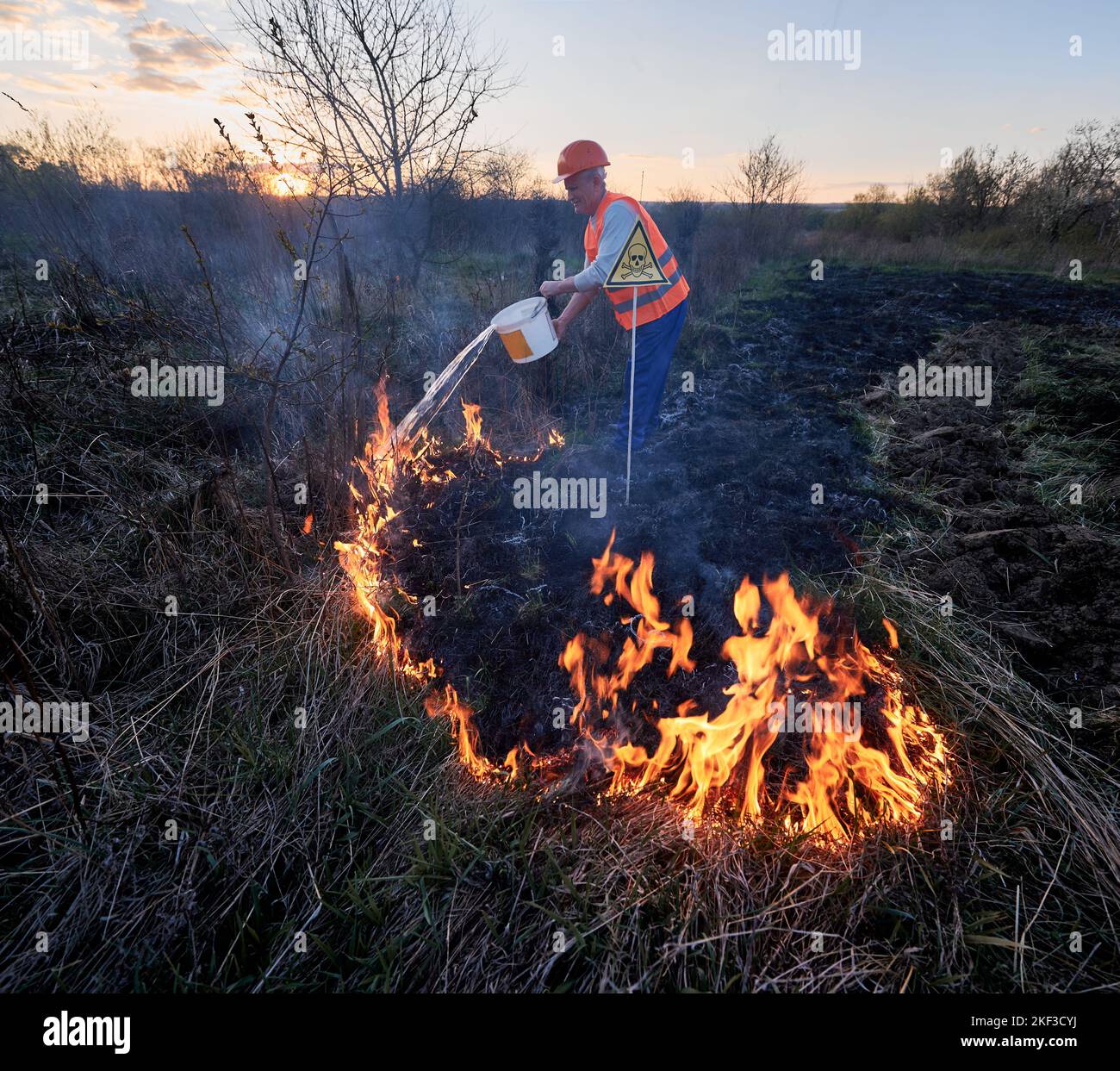 Fireman ecologist fighting wildfire in field with evening sky on ...