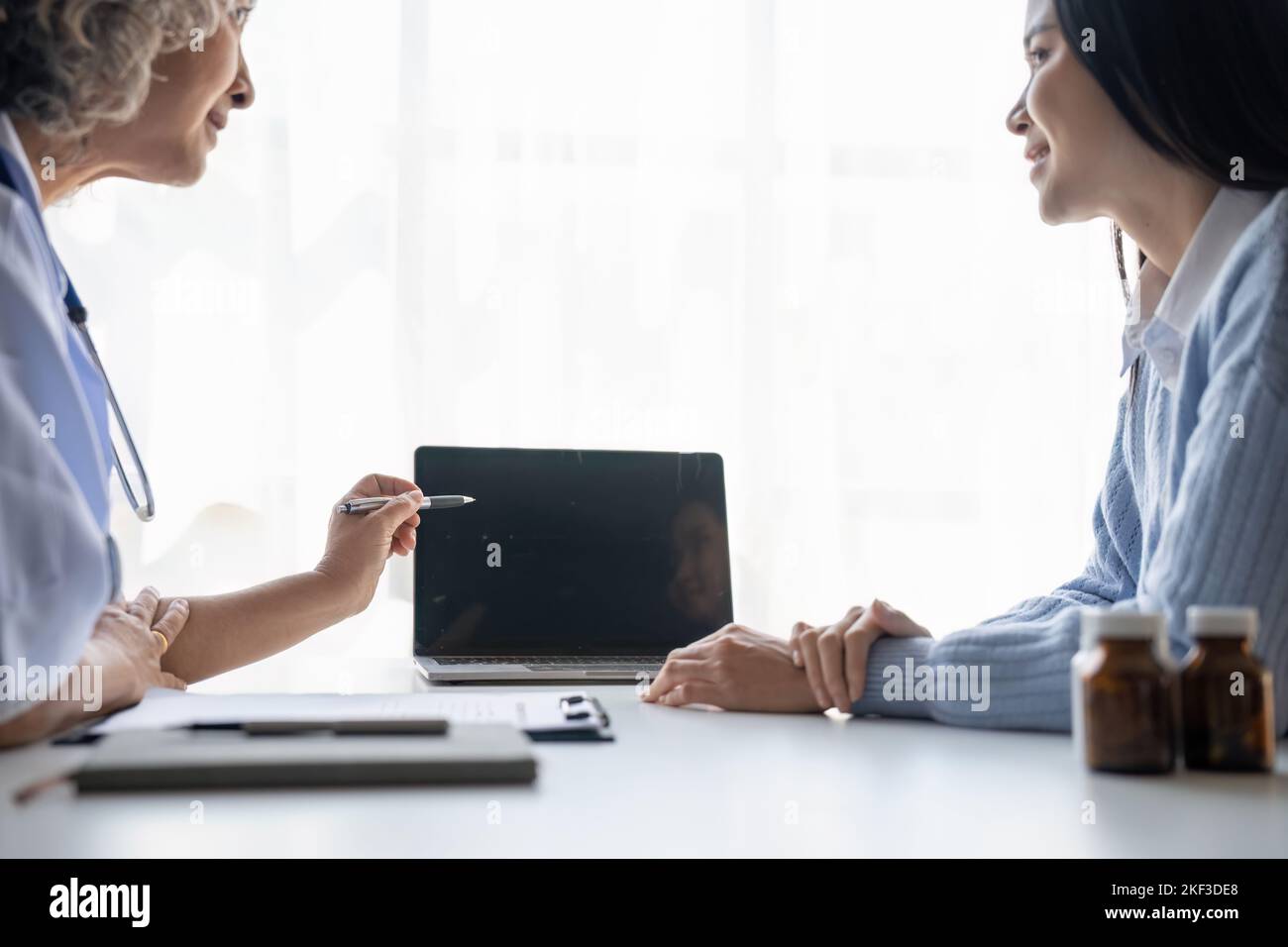 Woman senior doctor consults her female patient in clinic on laptop ...