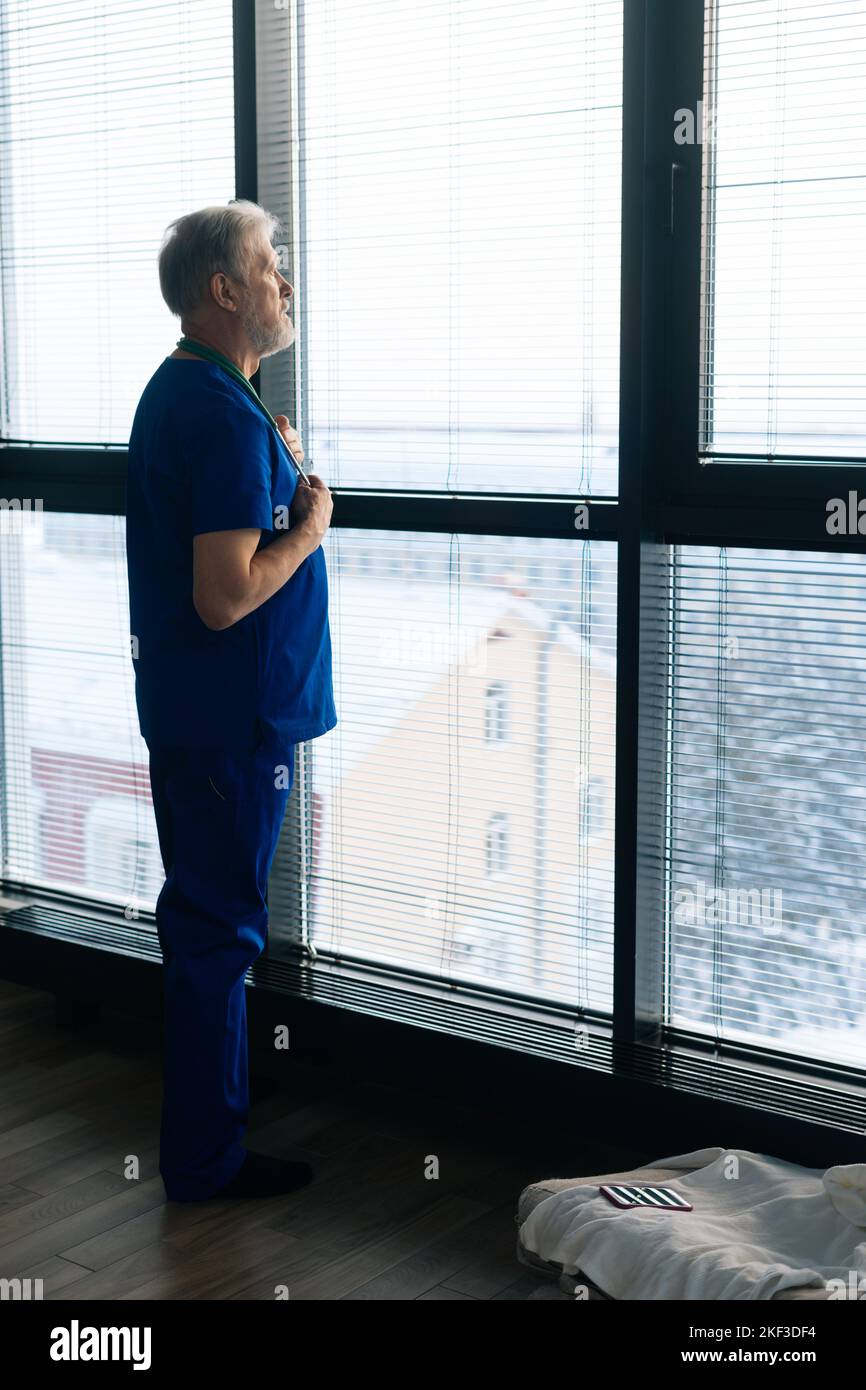 Vertical portrait of thoughtful mature male doctor looking outside ...