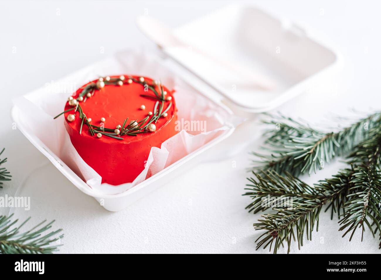 Bento cake red color in a white container next to a Christmas tree ...