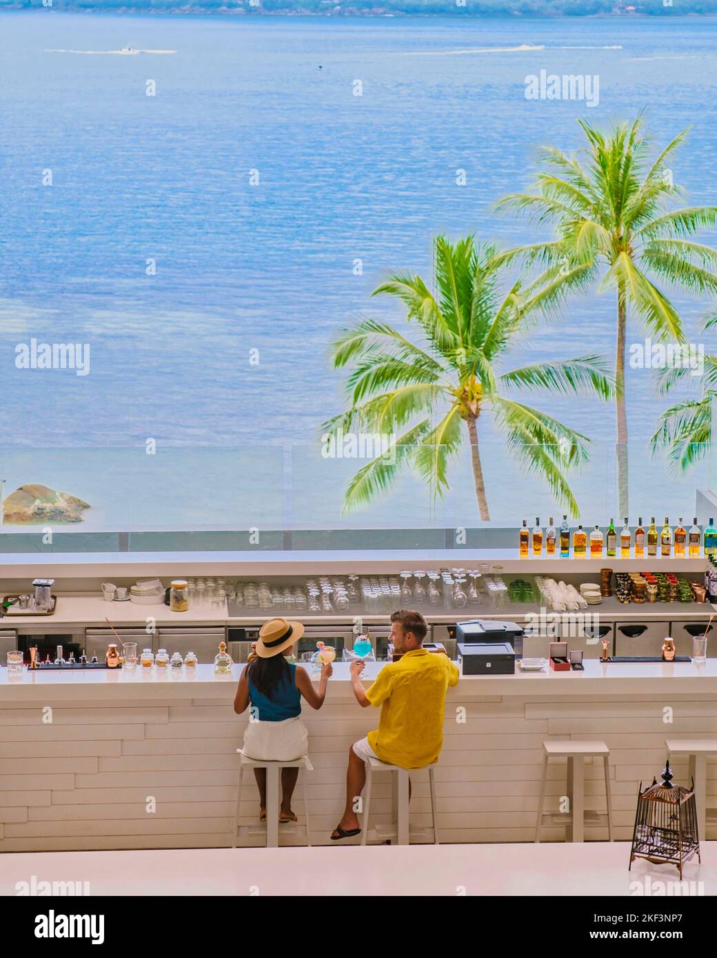 Couple drinking cocktails in the bar looking out over a blue ocean with ...
