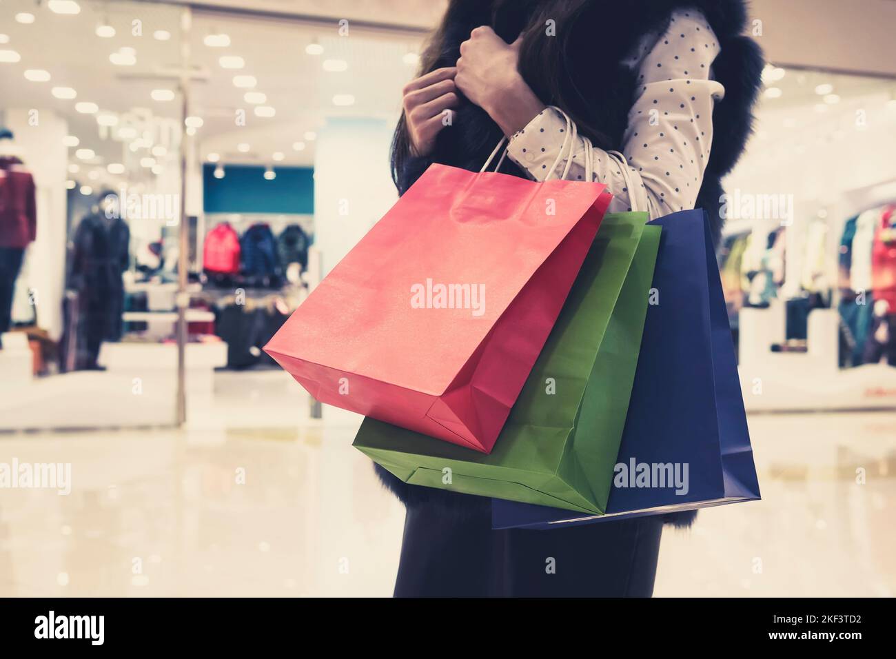 Young slender woman in white blouse and fur waistcoat holding shopping ...