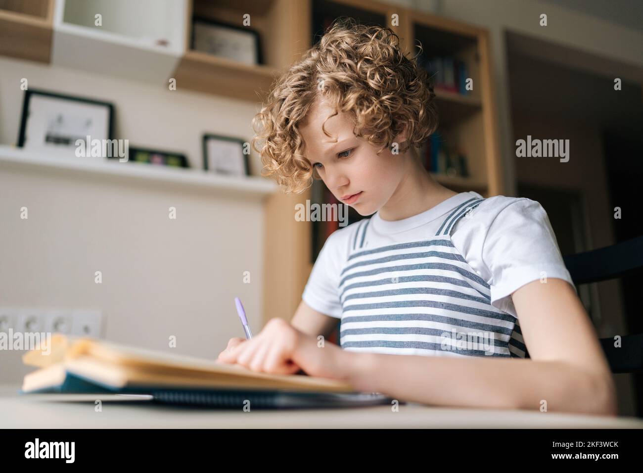 Low-angle view of concentrated little child schoolgirl writing in exercise book doing some ...
