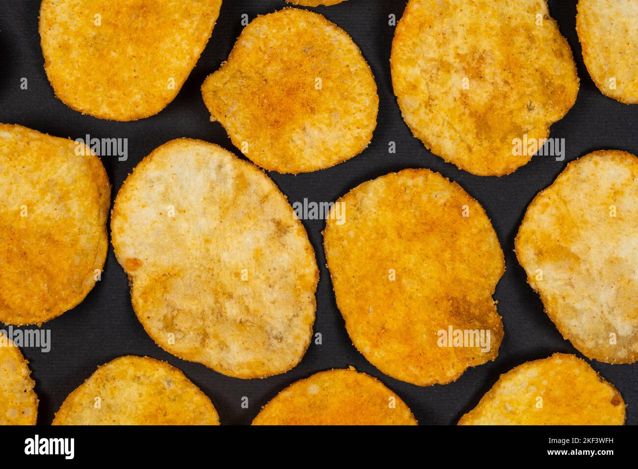 Delicious crispy potato chips with spices on a black background, top ...