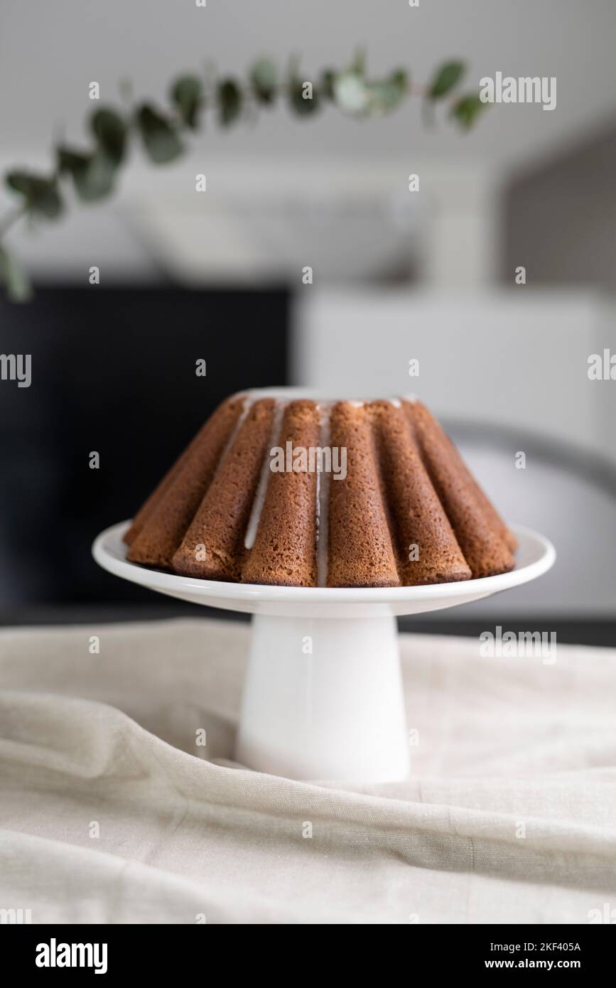 A vertical shot of a bundt brown cake with a white topping on a cake ...