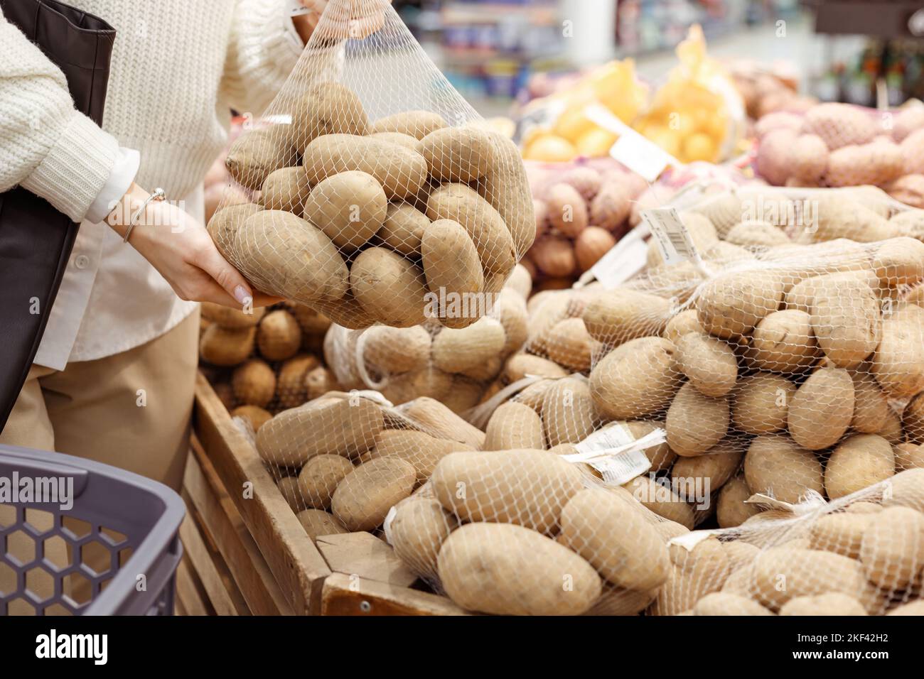 Woman puts mesh bag with potato into trolley for purchases in ...