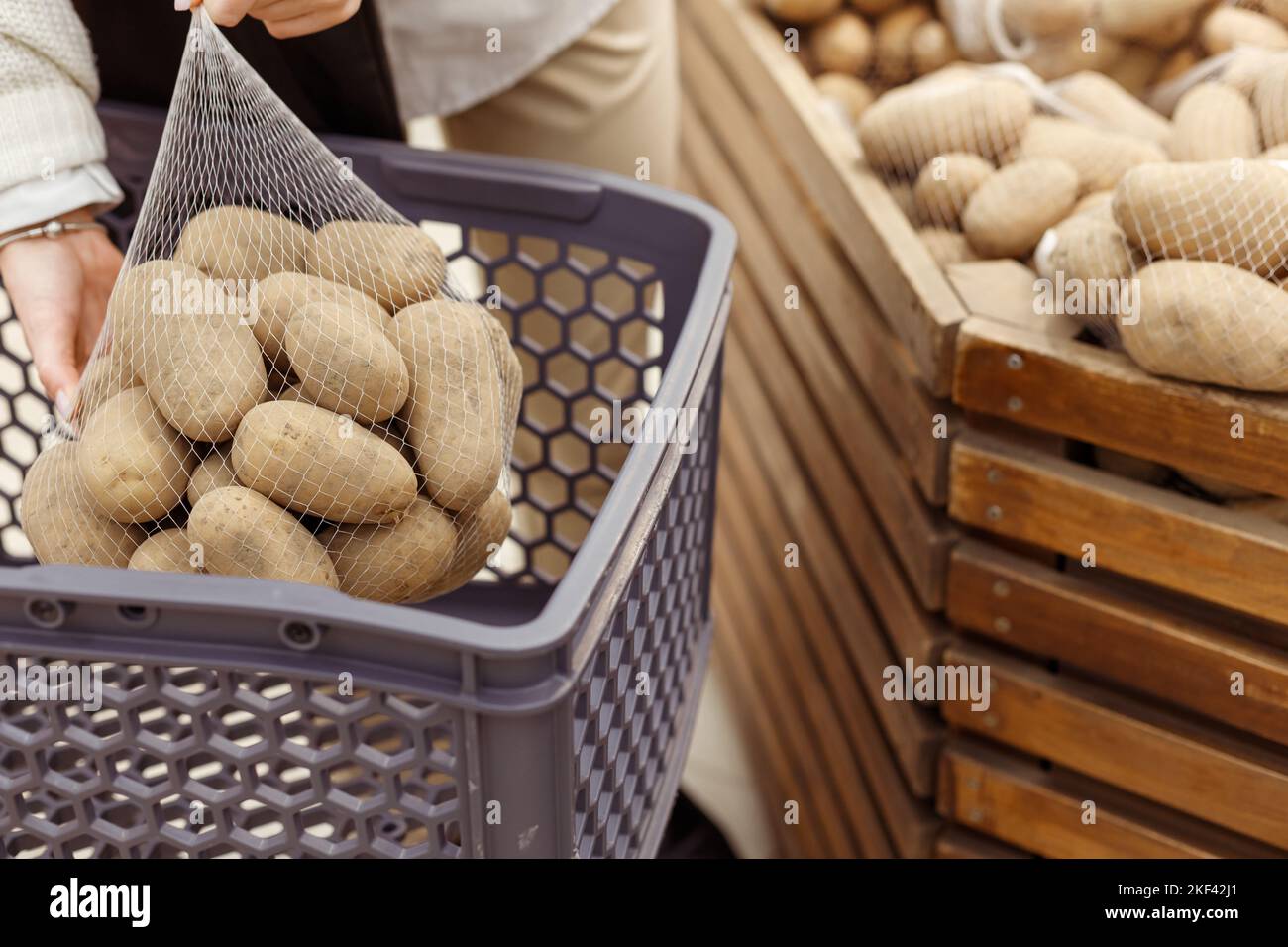 Woman puts mesh bag with potato into trolley for purchases in ...