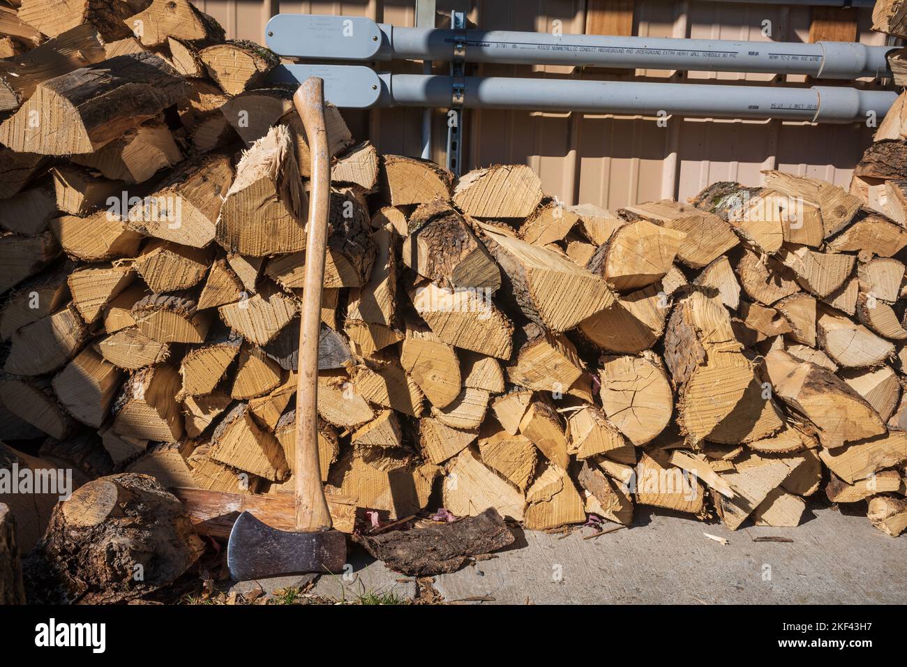 A still-life of a stack of chopped wood and an axe along the side of a ...