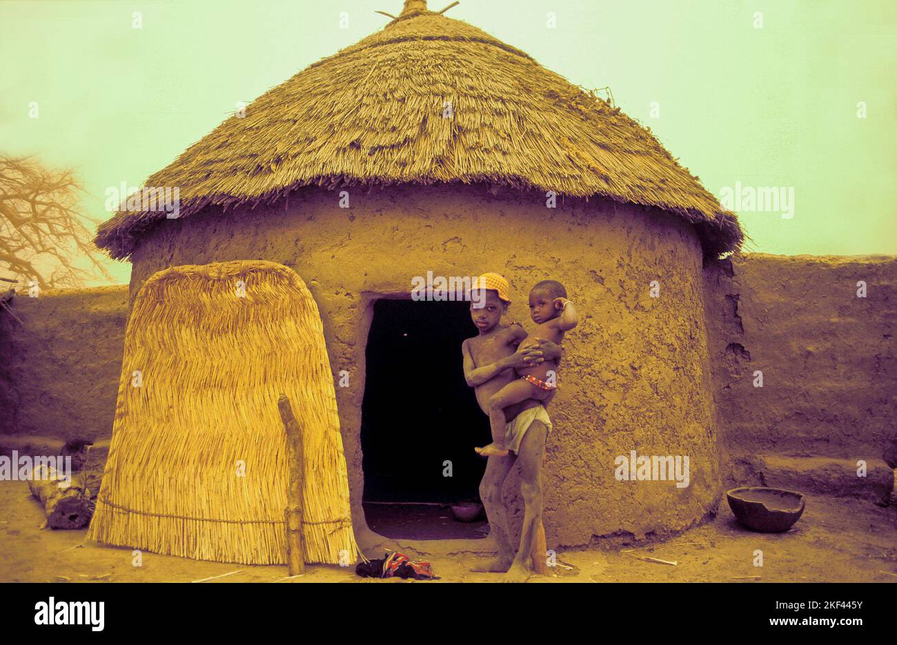 Burkina Faso, Boy with baby standing in front of traditional loam or ...
