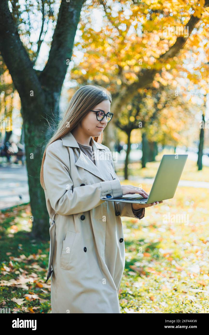 A cute woman in glasses with long hair is walking in an autumn park ...