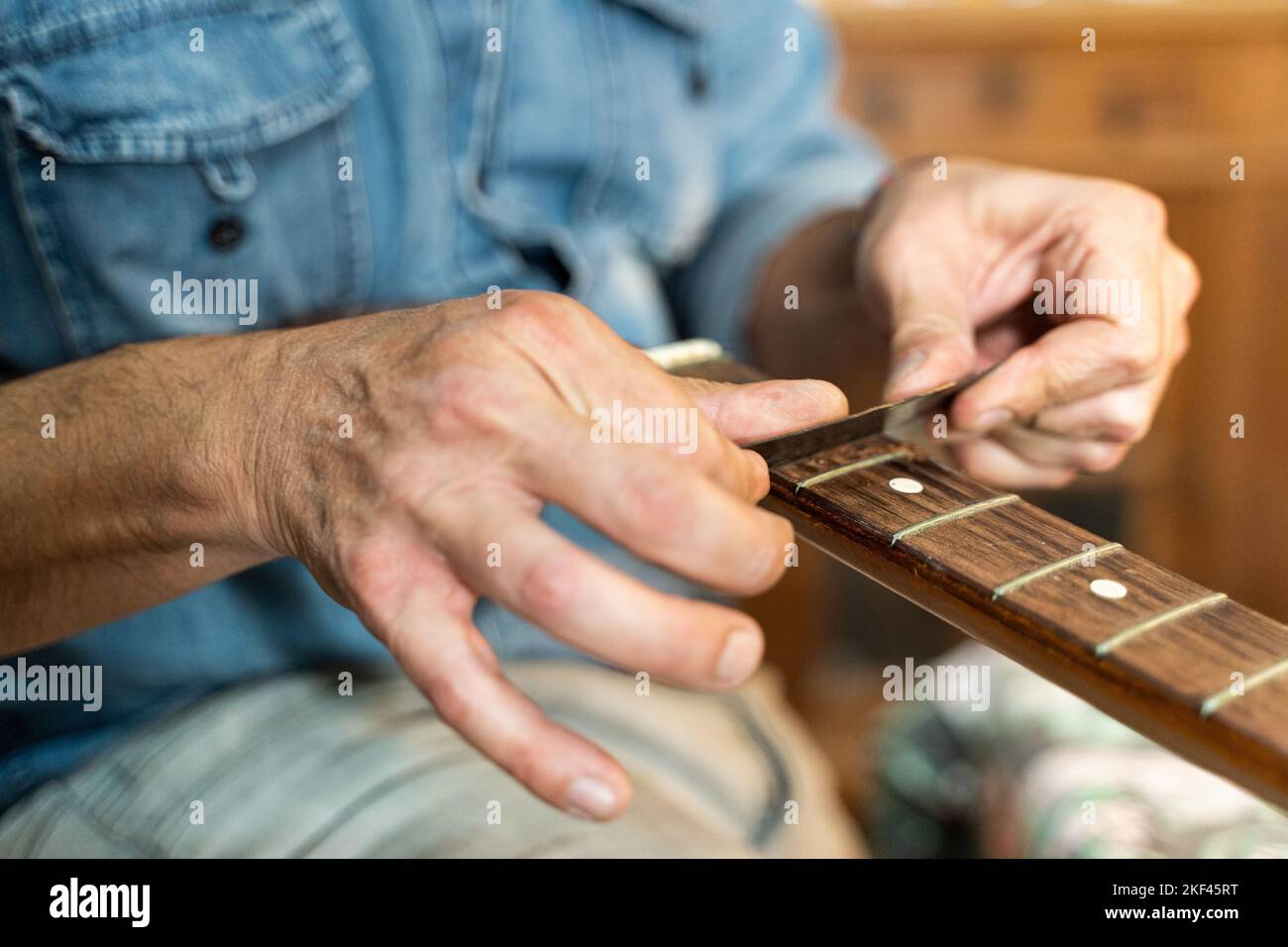 A luthier scrapes dirt off the fretboard of a guitar - cropped frame ...