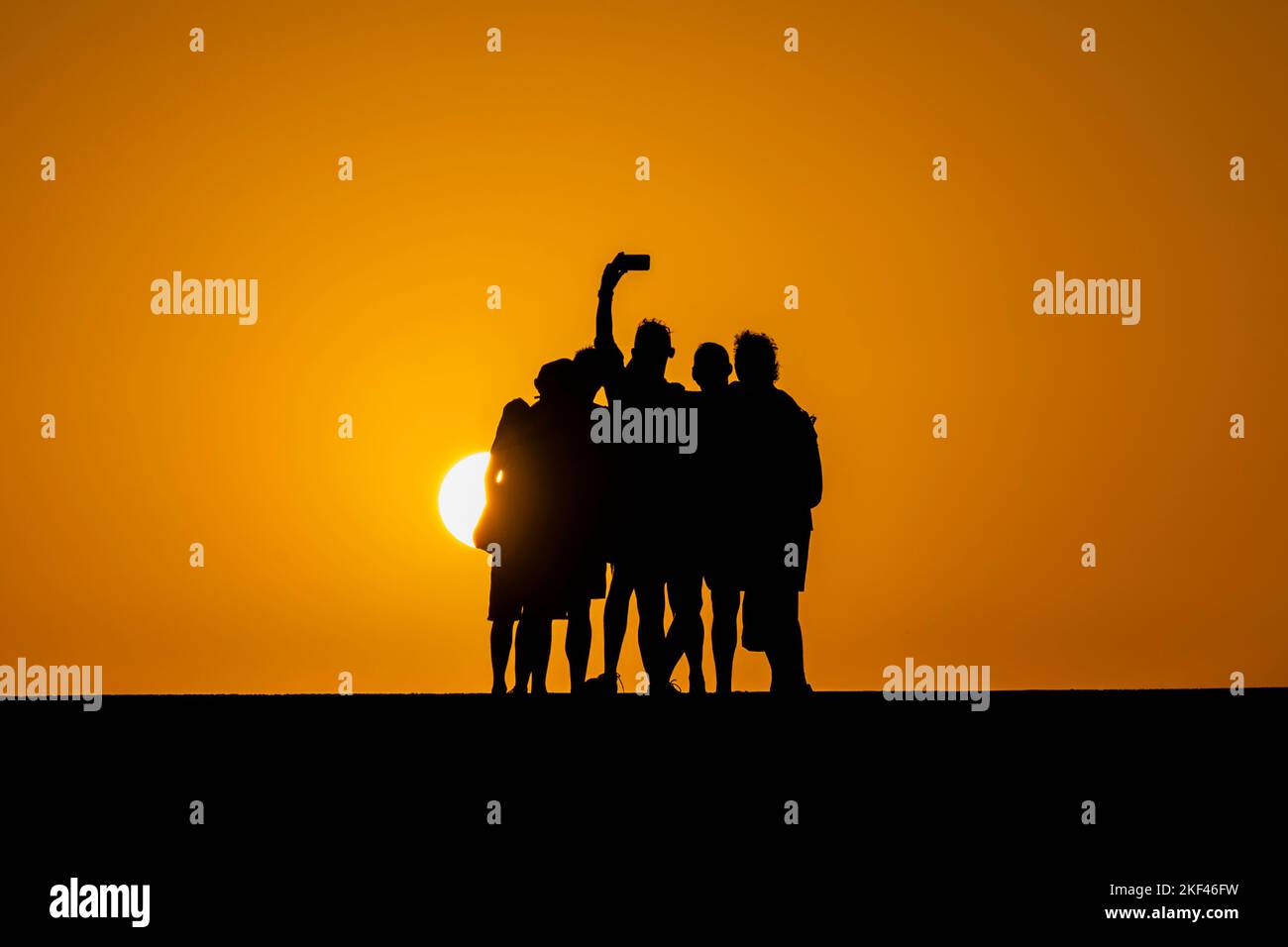 A backlight photo of a group of people taking a selfie at sunset ...