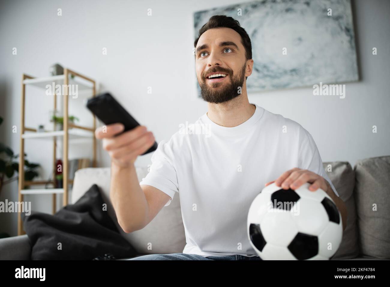 happy man holding football and remote controller while watching ...