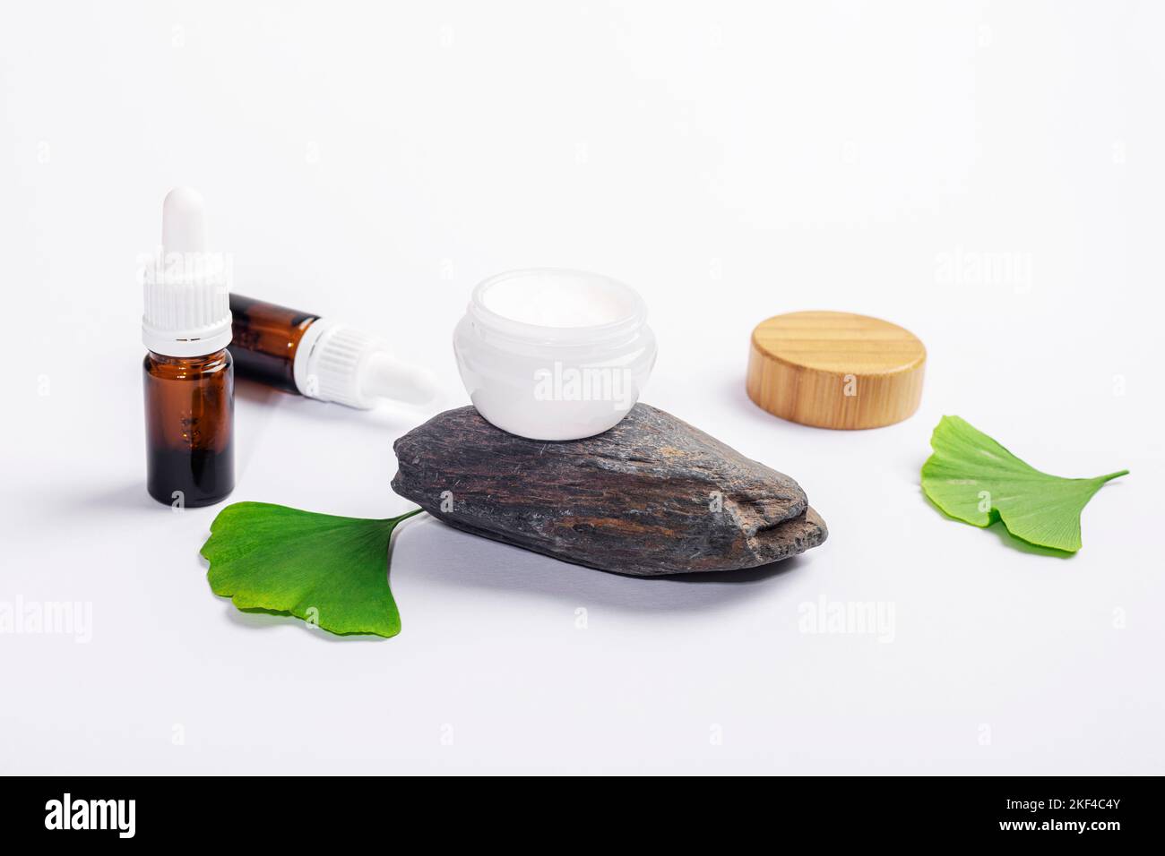 Fresh green ginkgo leaves, cream jar on a natural stone, brown glass ...