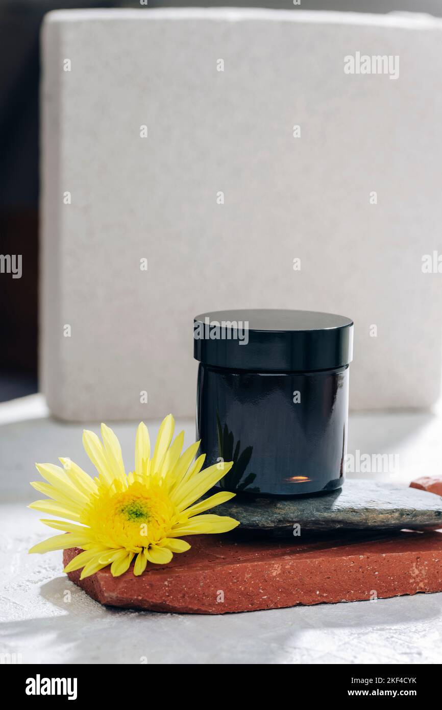 Black cream jar and yellow flower on natural stone background. Skincare ...