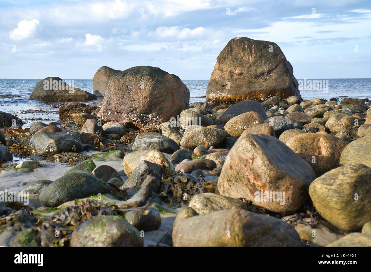 Big stones on stone beach in front of sea with clouds in sky. Denmark ...