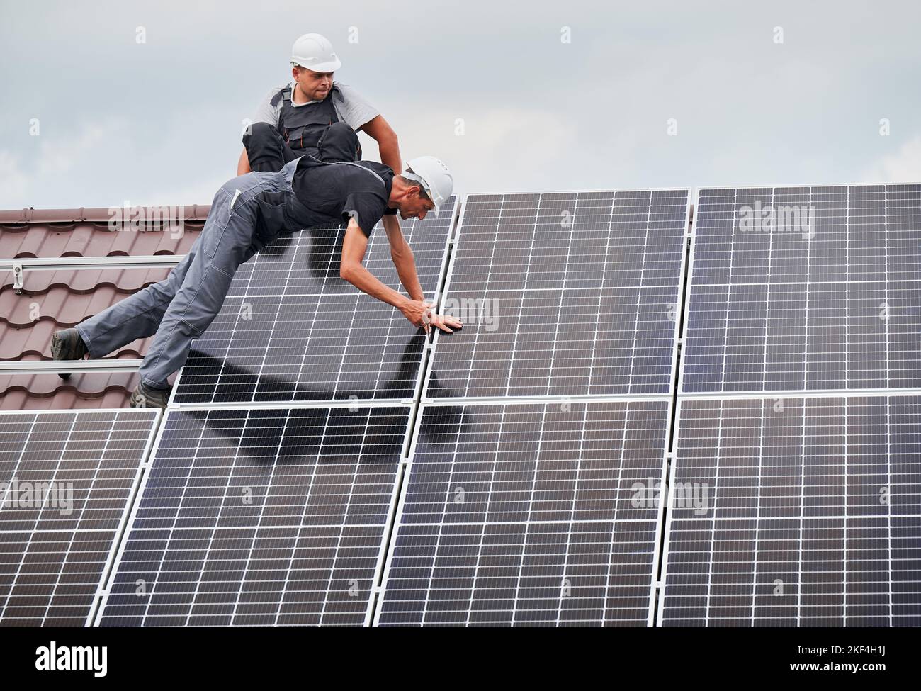 Men installers mounting photovoltaic solar moduls on roof of house ...