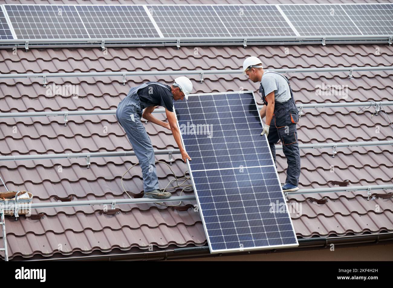 Men technicians lifting up photovoltaic solar moduls on roof of house ...