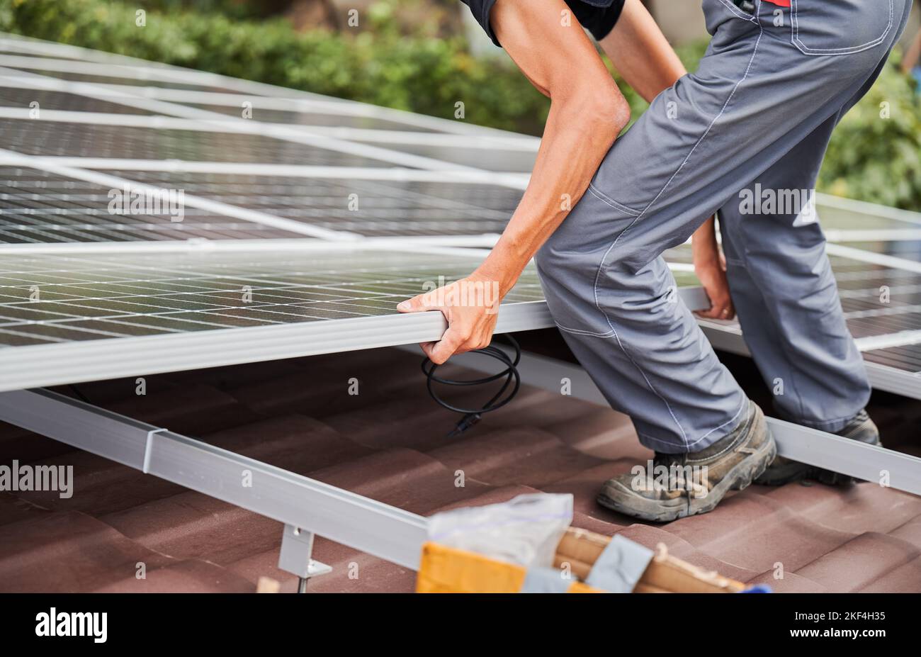 Man technician mounting photovoltaic solar moduls on roof of house. Cropped view of electrician ...