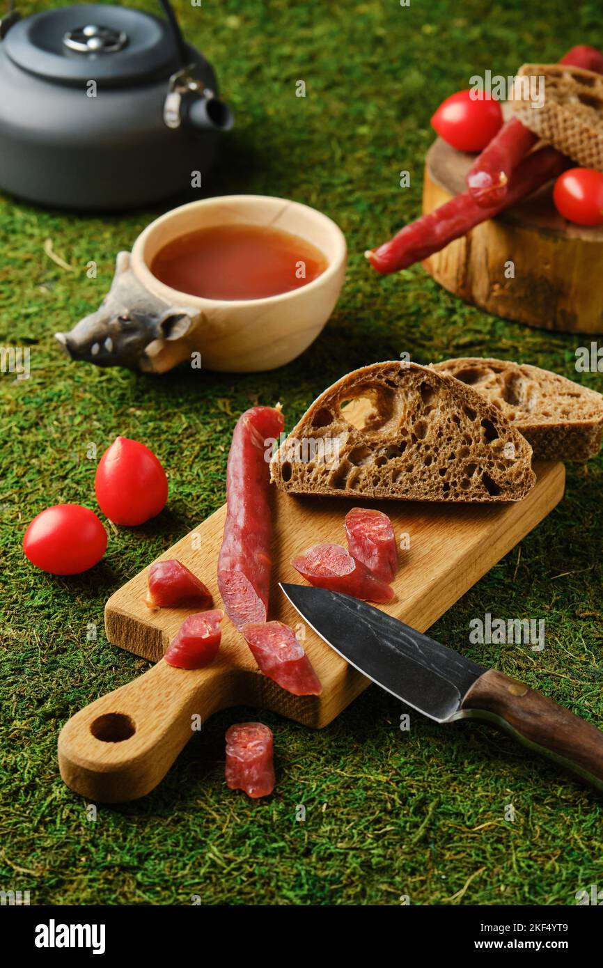 Snack in the woods with dried thin sausage, bread and tomatoes on the ...