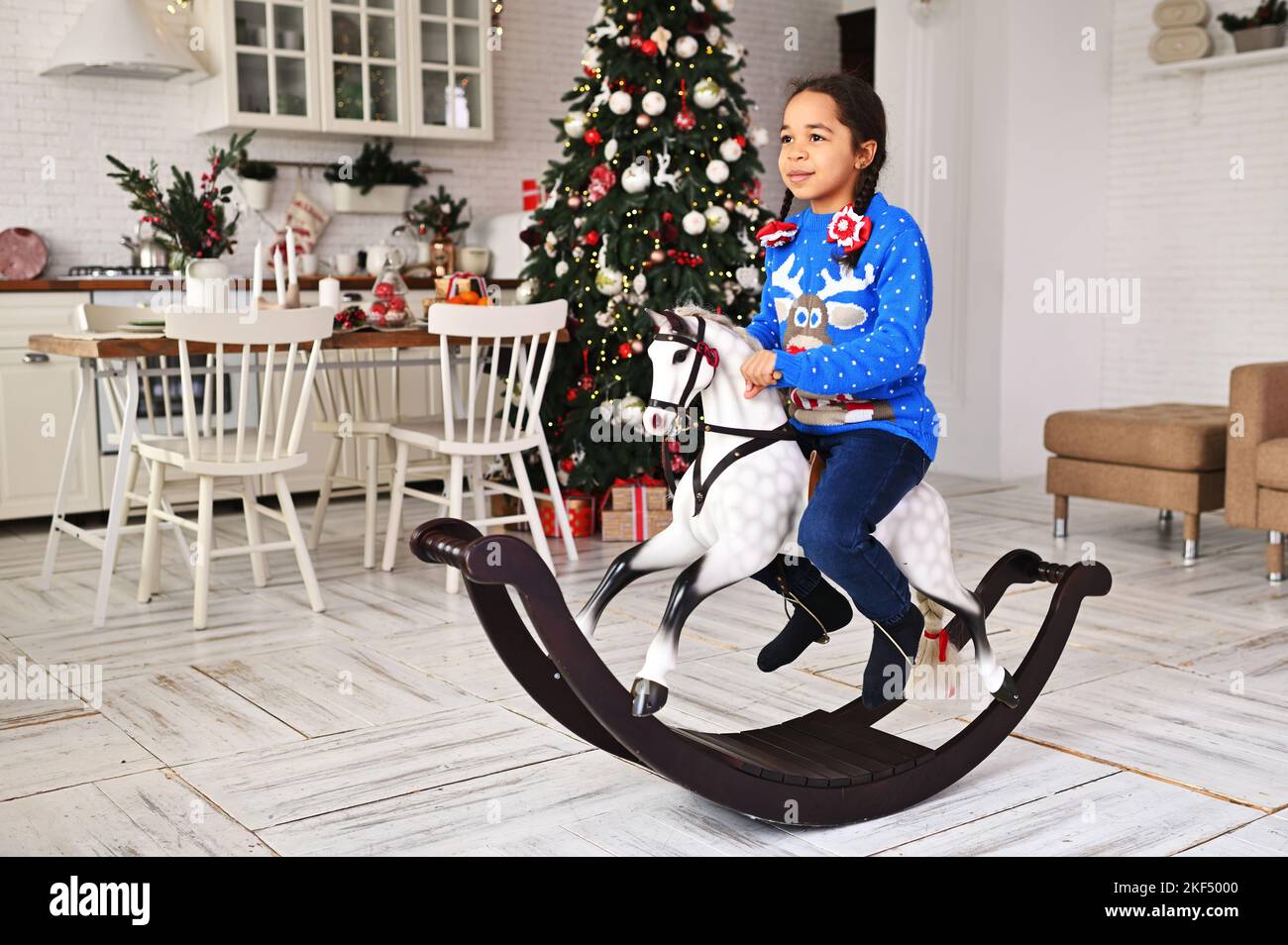 little African-American girl in a blue Christmas sweater smiles while ...