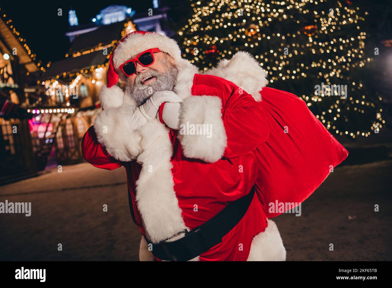 Photo of funky cheerful santa carry big presents bag evergreen tree ...