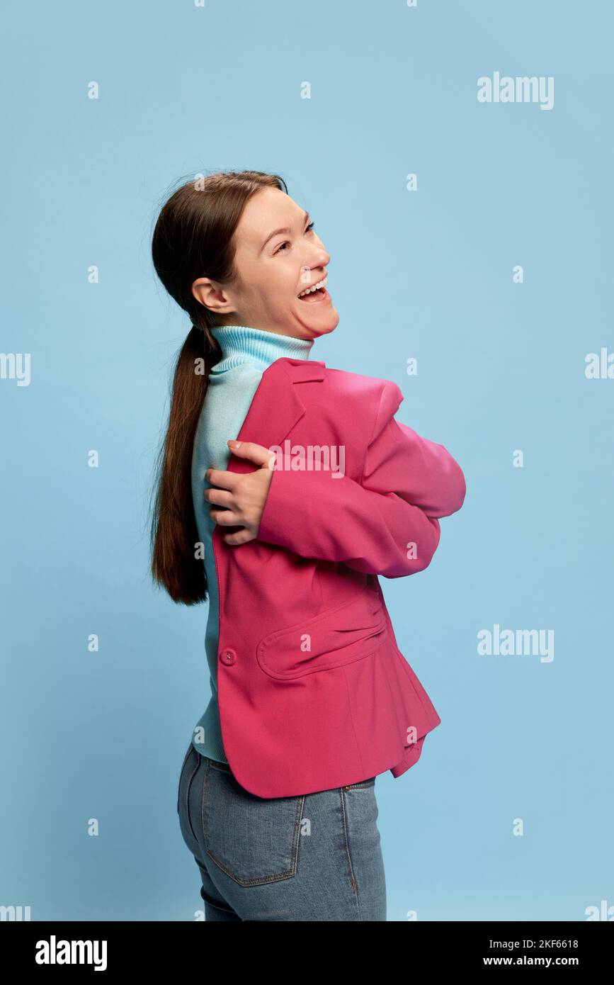 Portrait of young woman posing in pink jacket, hugging herself isolated ...