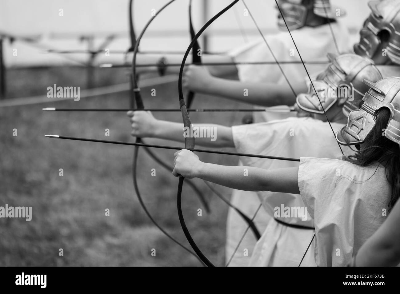A grayscale shot of a group of people firing arrows with bows at a ...