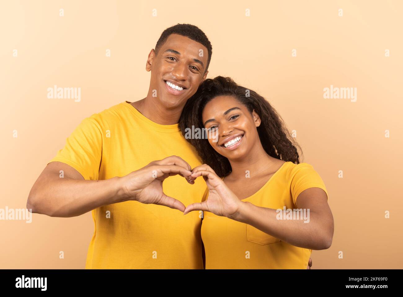Loving african american couple cuddling and making together heart shape gesture with their hands ...