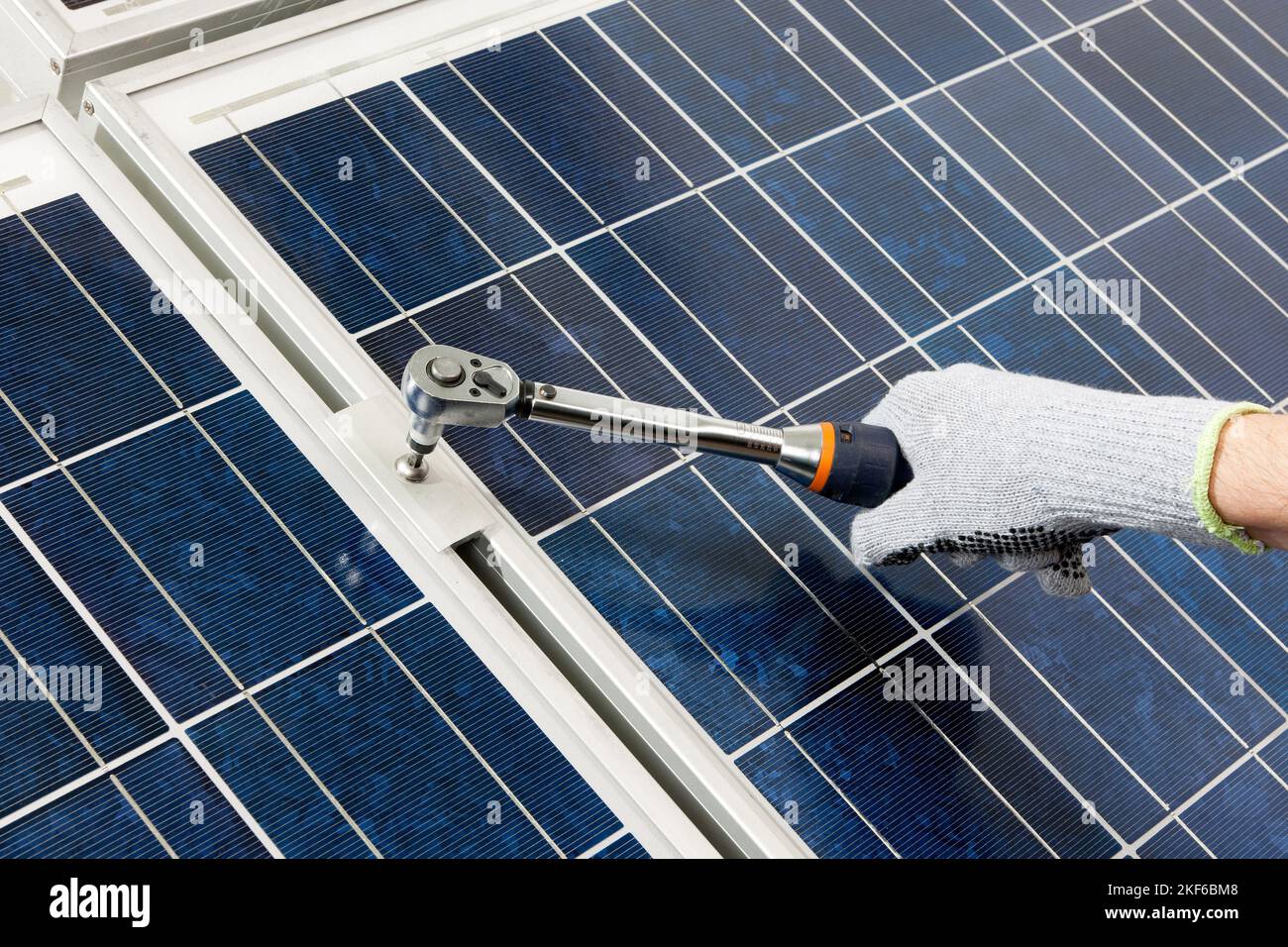 A worker's hand screws solar panels onto a roof with a torque wrench in ...