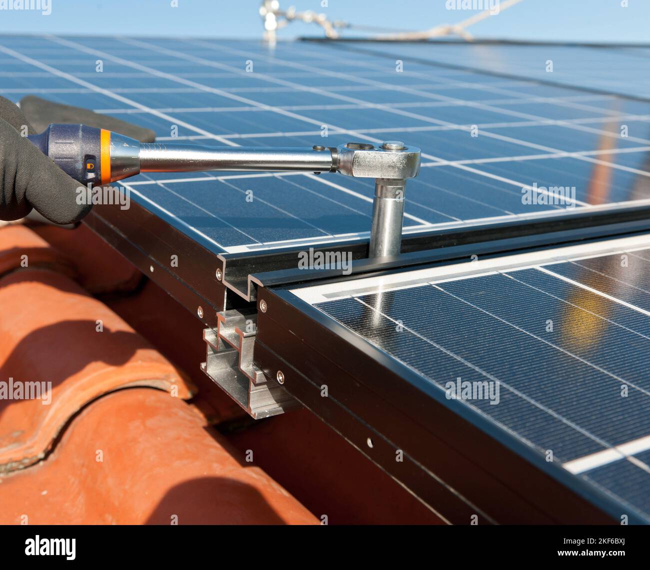 A worker's hand screws solar panels onto a red tile roof with a torque ...