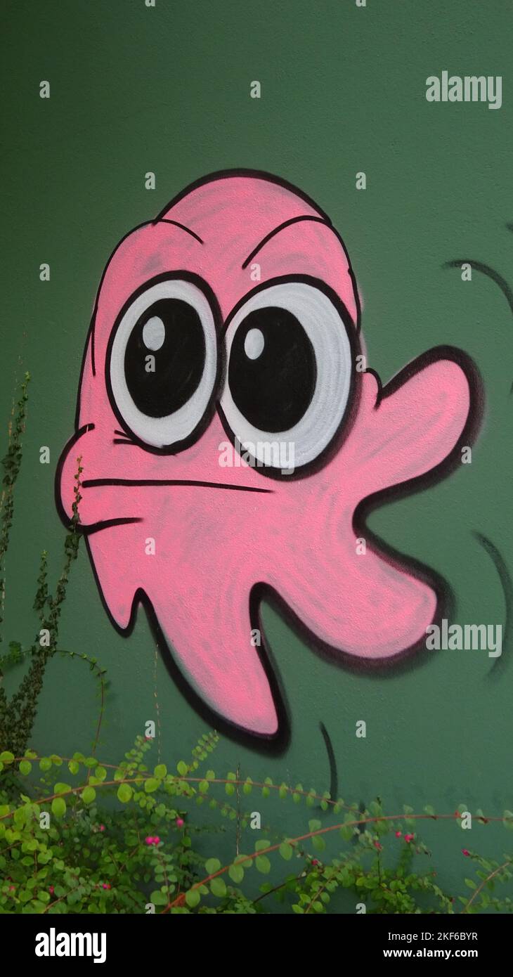A vertical shot of a painted cute pink octopus graffiti on a green wall ...