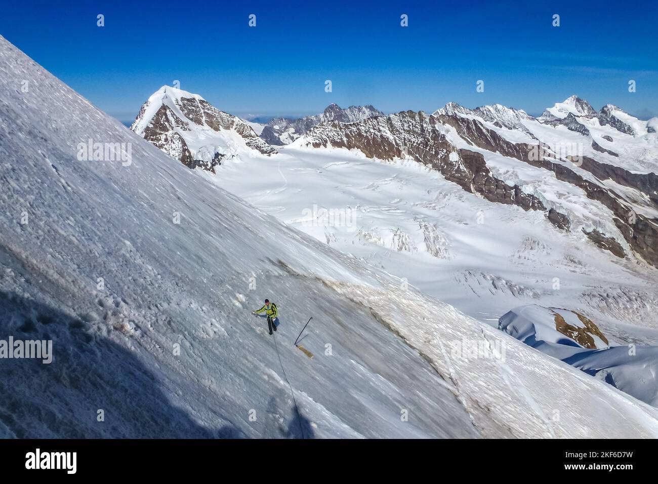 Description: Mountaineer secured by rope hikes over a steep snow slope ...