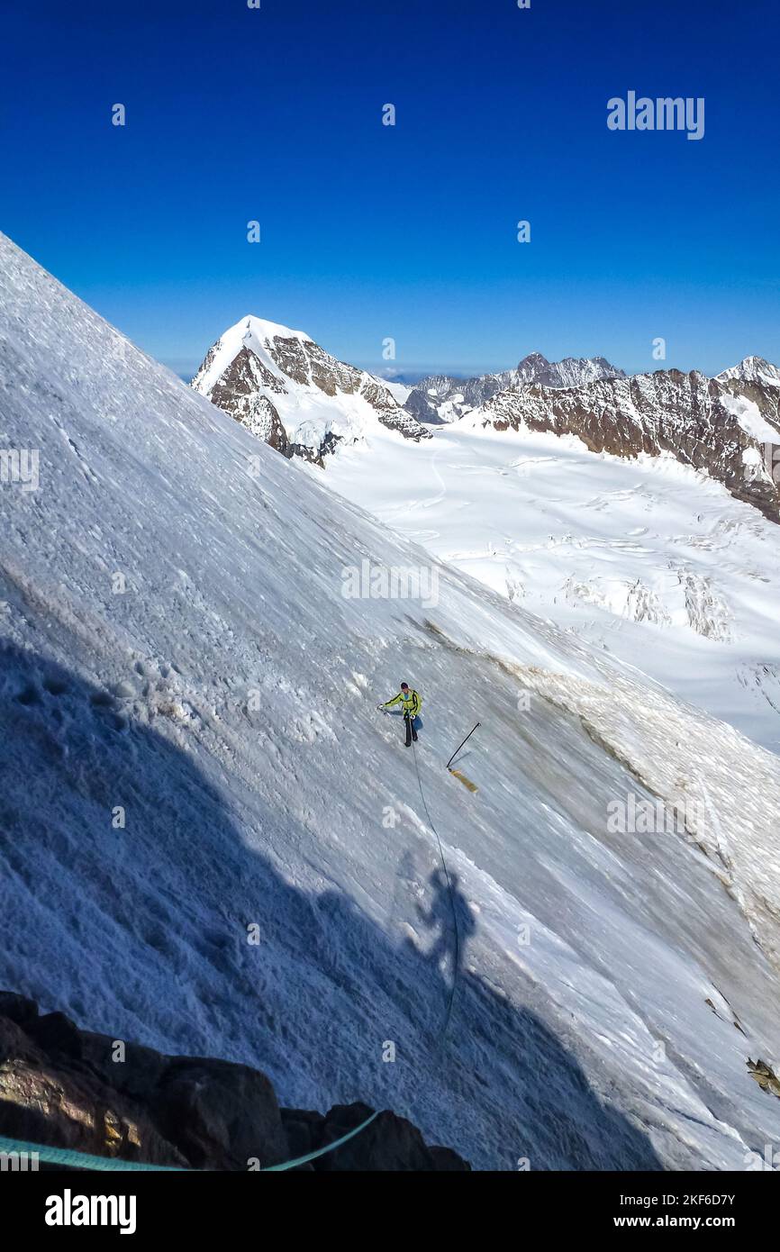 Description: Mountaineer secured by rope hikes over a steep snow slope ...