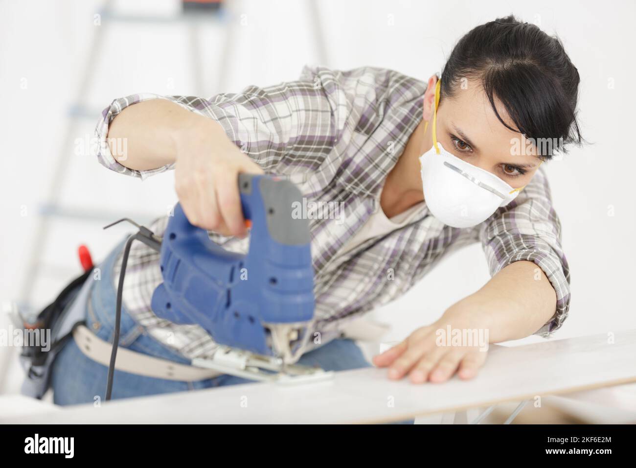 female carpenter wearing dust mask while using electric jigsaw Stock ...