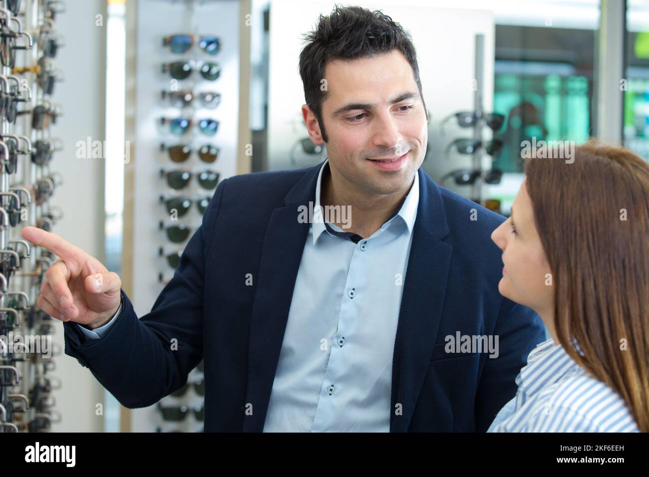 customer in opticians shop choosing frames being guided by salesman ...