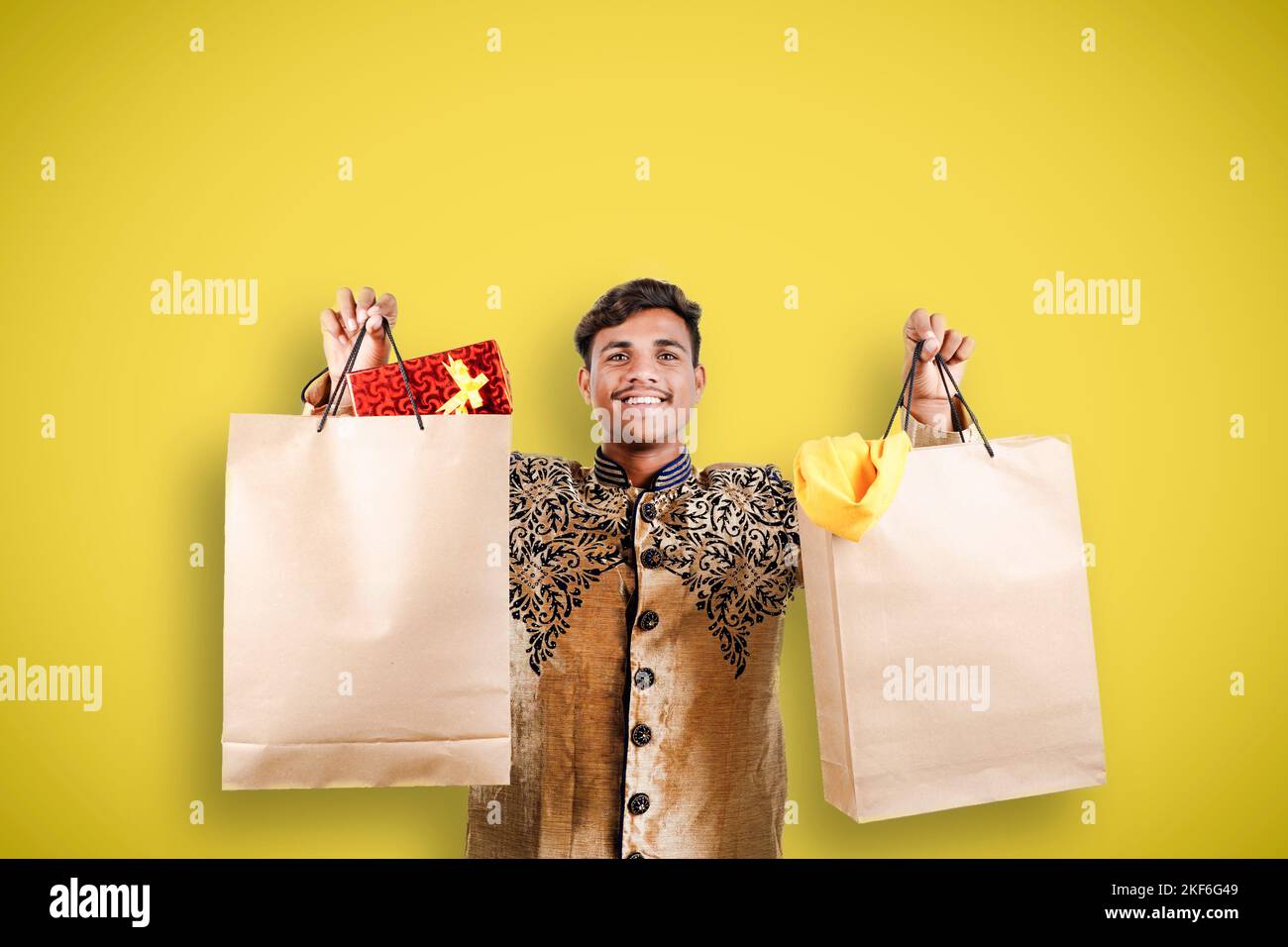 Indian man in ethnic wear with shopping bags, isolated over yellow ...