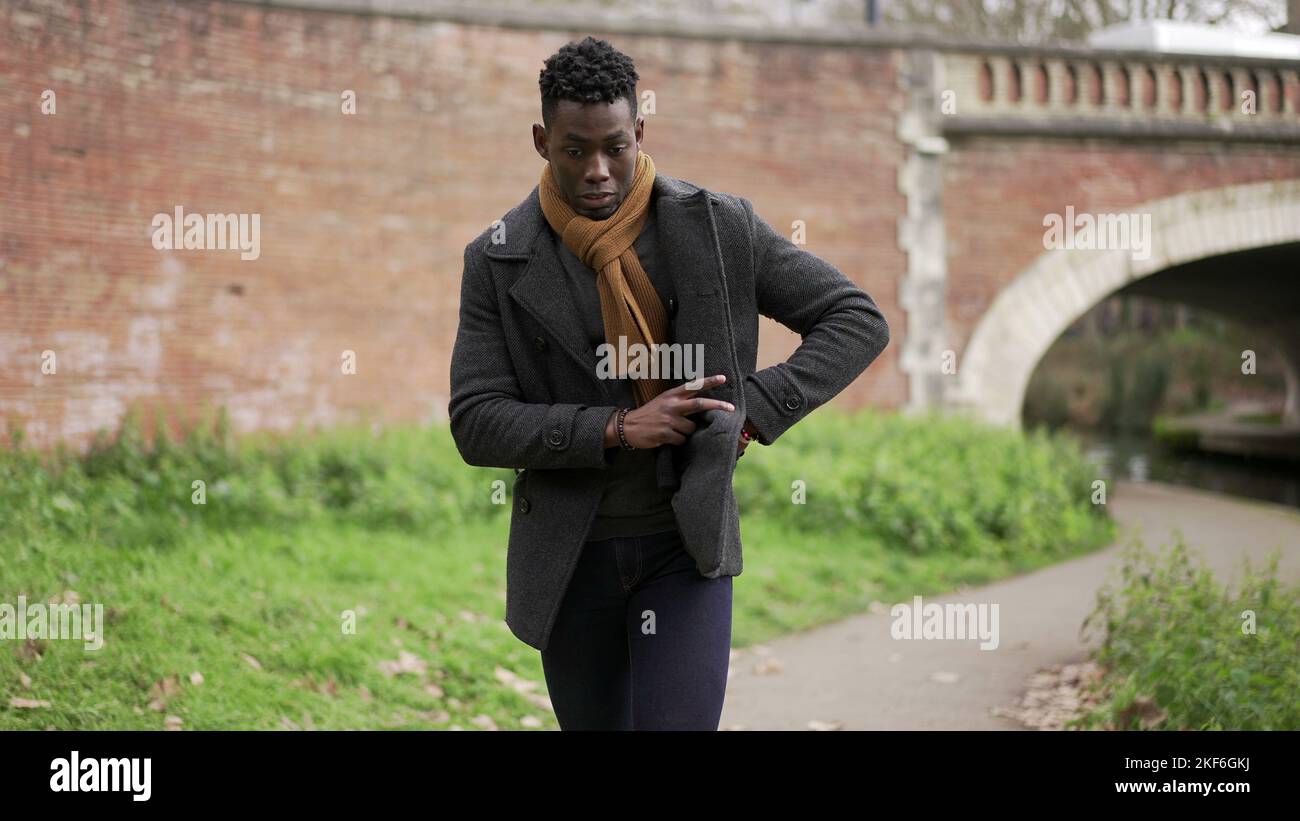 Black man walking outside during winter season putting on gloves ...