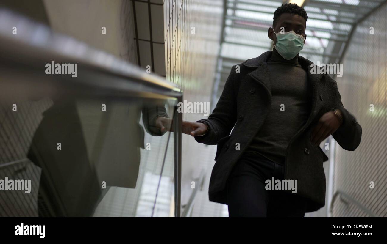 Black man wearing covid mask descending metro subway stairs touching ...