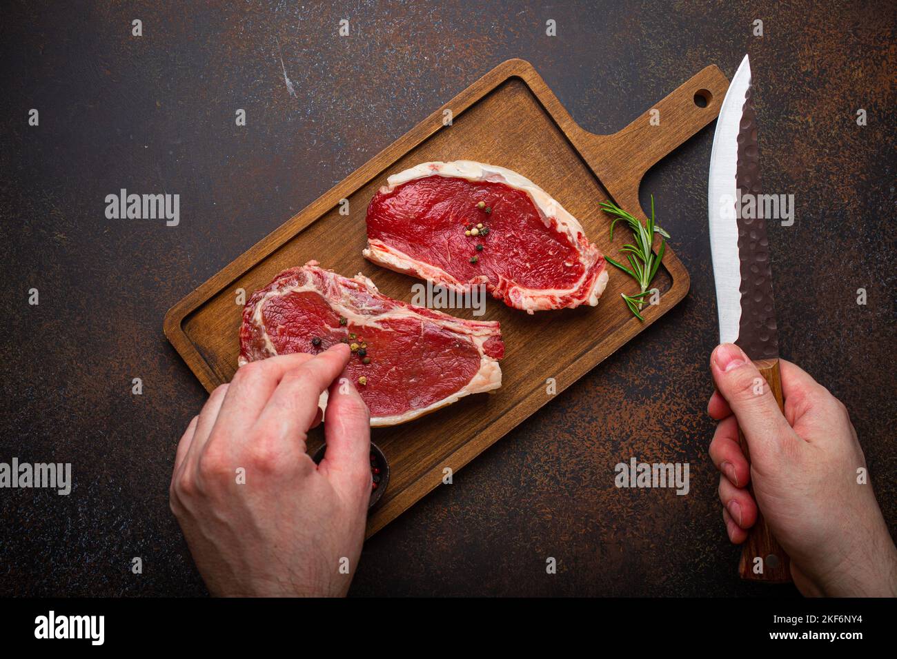 Male's hand holding knife over two raw meat beef steaks top view Stock ...